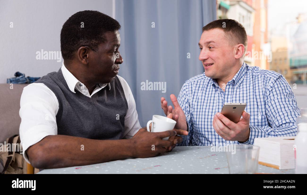 Men enjoying conversation at home, using phone Stock Photo - Alamy