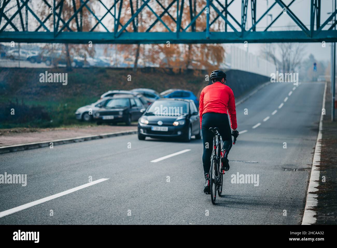 A back view of a young cool male cyclist in red sportswear riding a ...