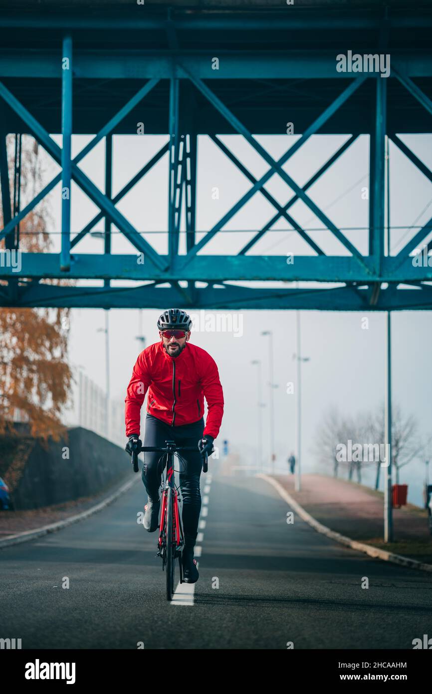Front view of a young cool male cyclist in red sportswear riding a ...