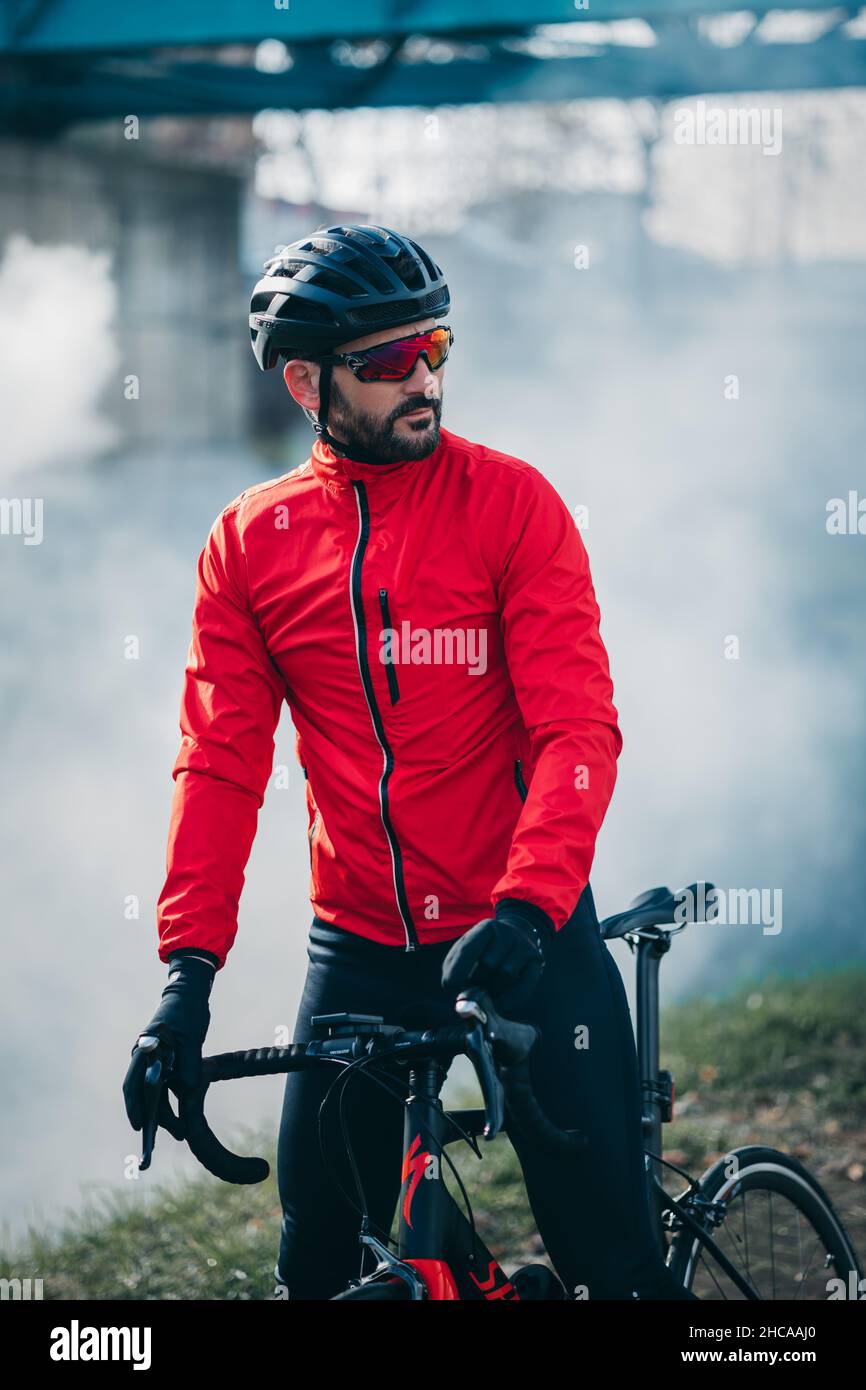 Side view of a young cool male cyclist in red sportswear riding a ...