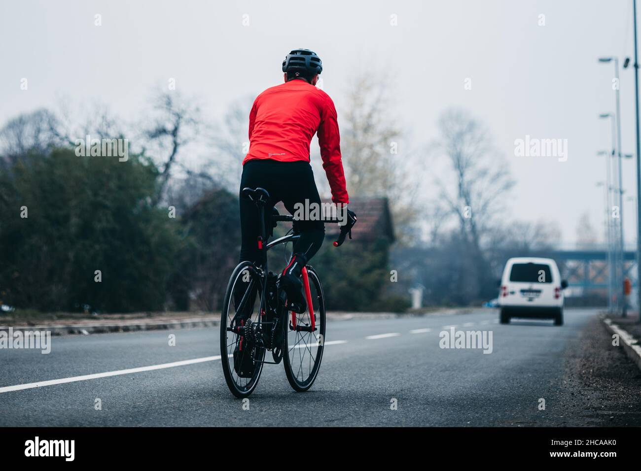 Back view of a young cool male cyclist in red sportswear riding a ...