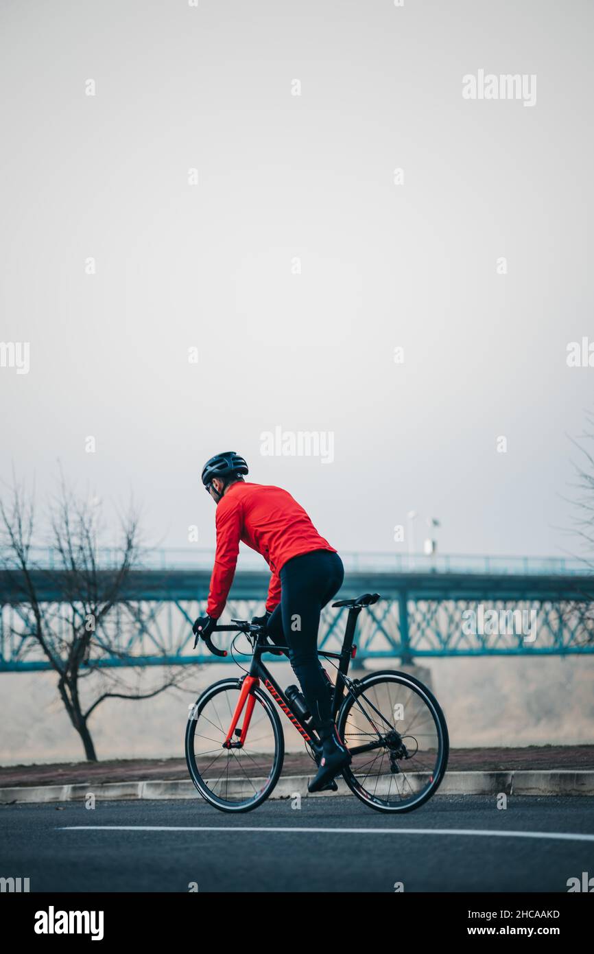 Side view of a young cool male cyclist in red sportswear riding a ...