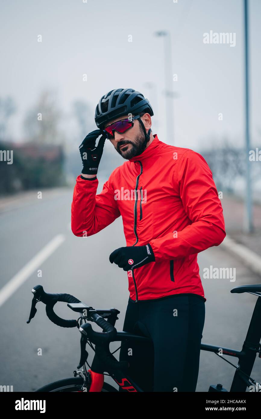 Young cool male cyclist in red sportswear adjusting his glasses during ...