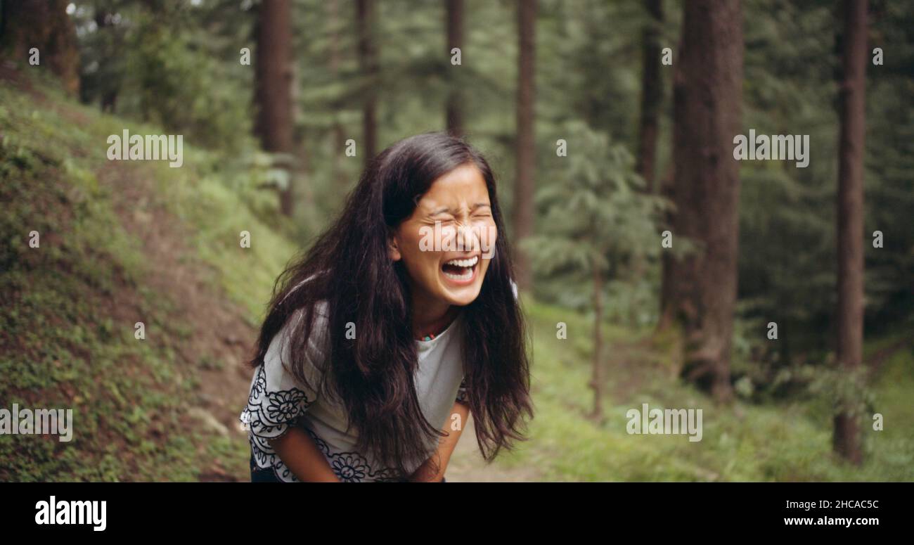 Indian female laughing hard in a forest with blurred trees background ...