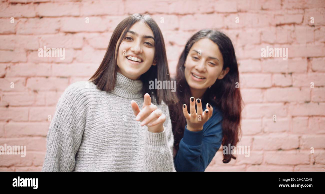 Closeup of two Indian females smiling with their hands up pointing ...