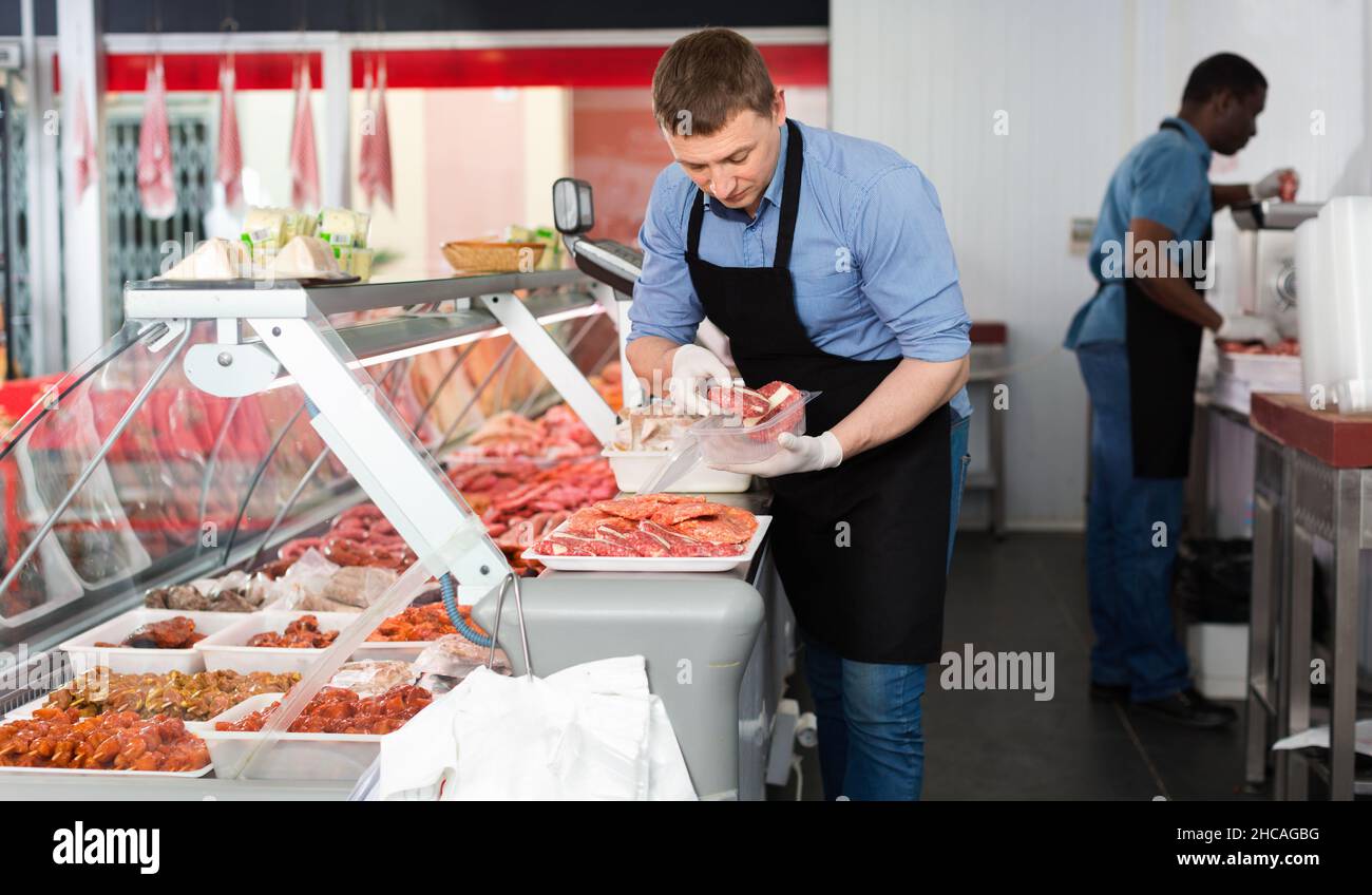 Successful owner of butcher store preparing fresh meat products for ...