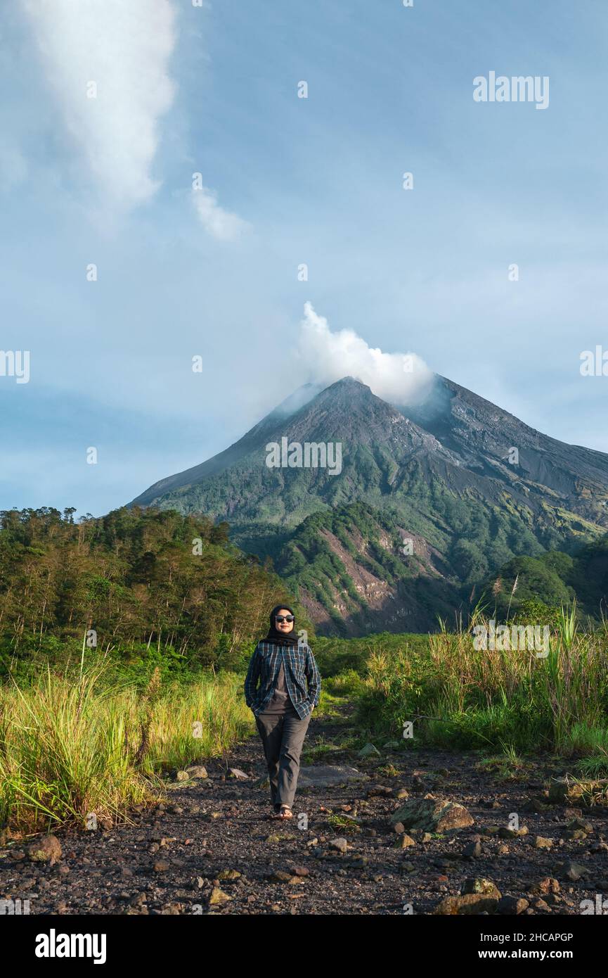 Lady on hijab walking toward the camera with volcano as background ...