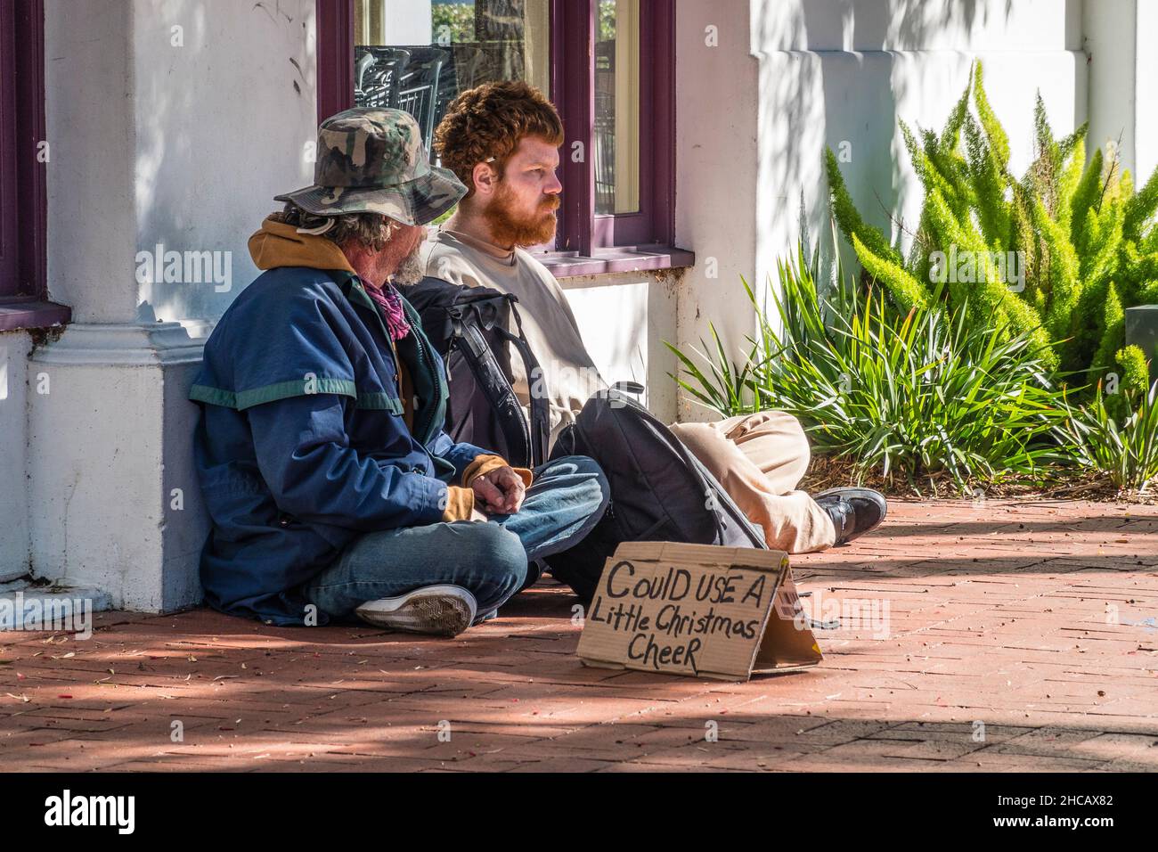 Two beggars sit on sidewalk with cardboard sign asking for Christmas ...
