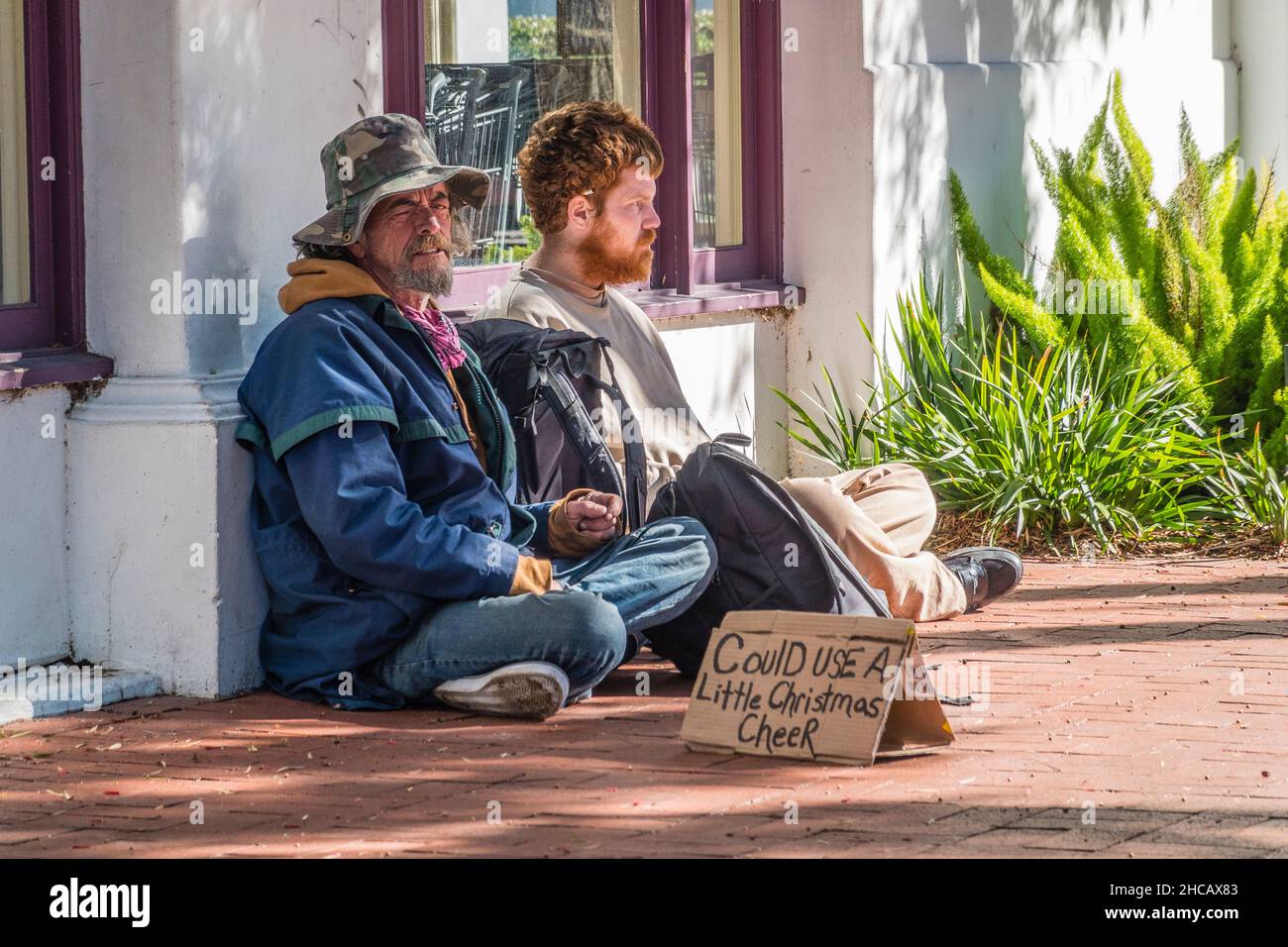 Two beggars sit on sidewalk with cardboard sign asking for Christmas ...