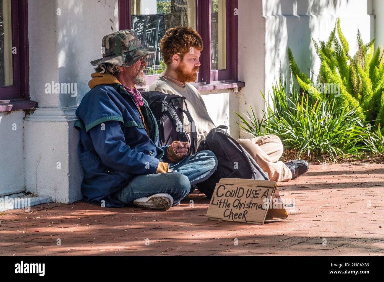 Two beggars sit on sidewalk with cardboard sign asking for Christmas ...