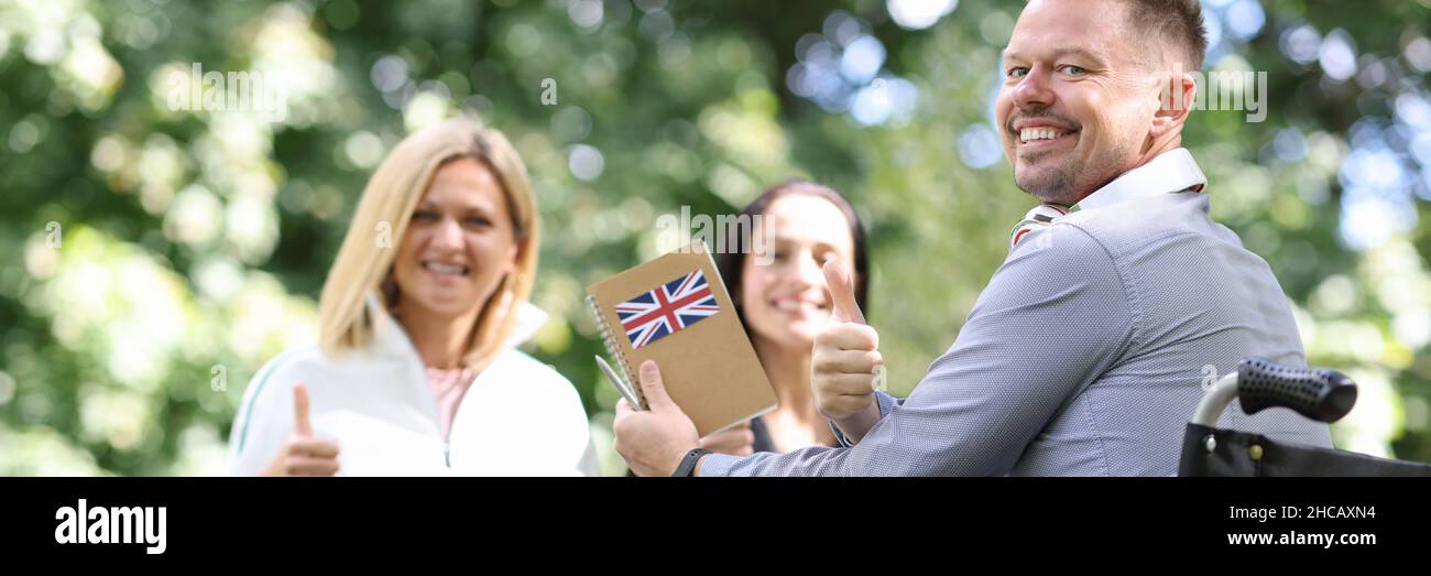Disabled man in wheelchair is studying English with girlfriends in park ...