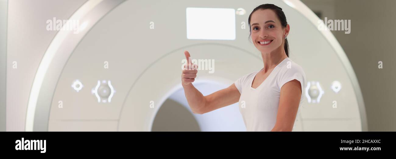 Young woman sitting on magnetic resonance imaging machine and showing ...
