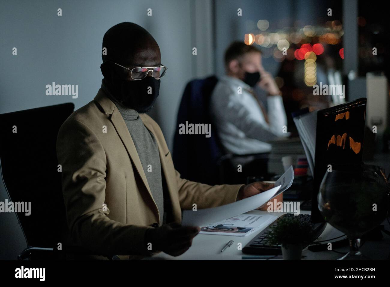 Young serious economist in protective mask looking through papers in ...