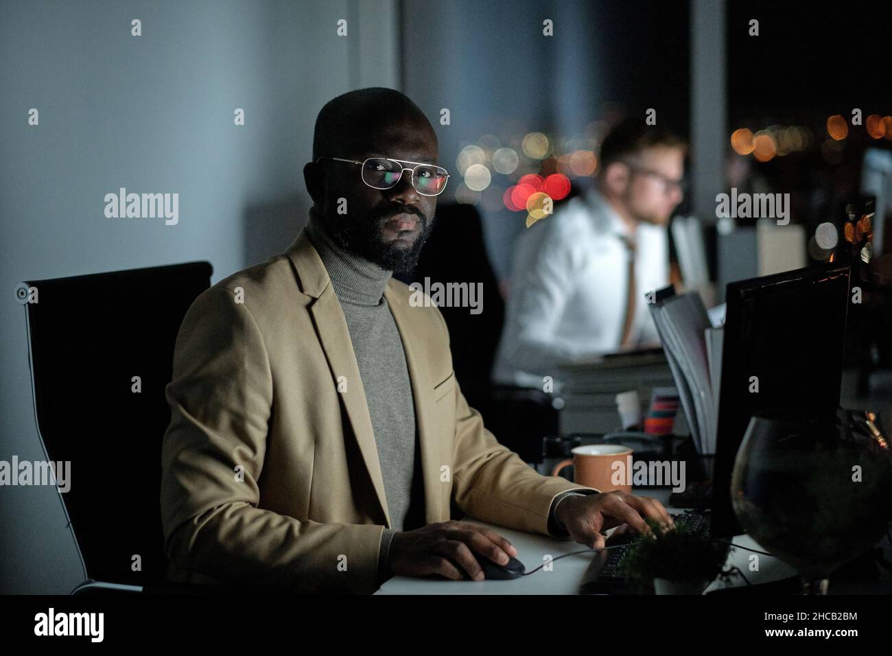 Young African broker in formalwear sitting in front of computer while ...