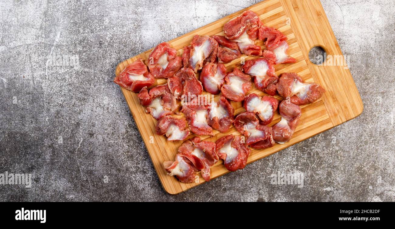 Raw chicken gizzards on a rectangular cutting wooden board on a dark ...