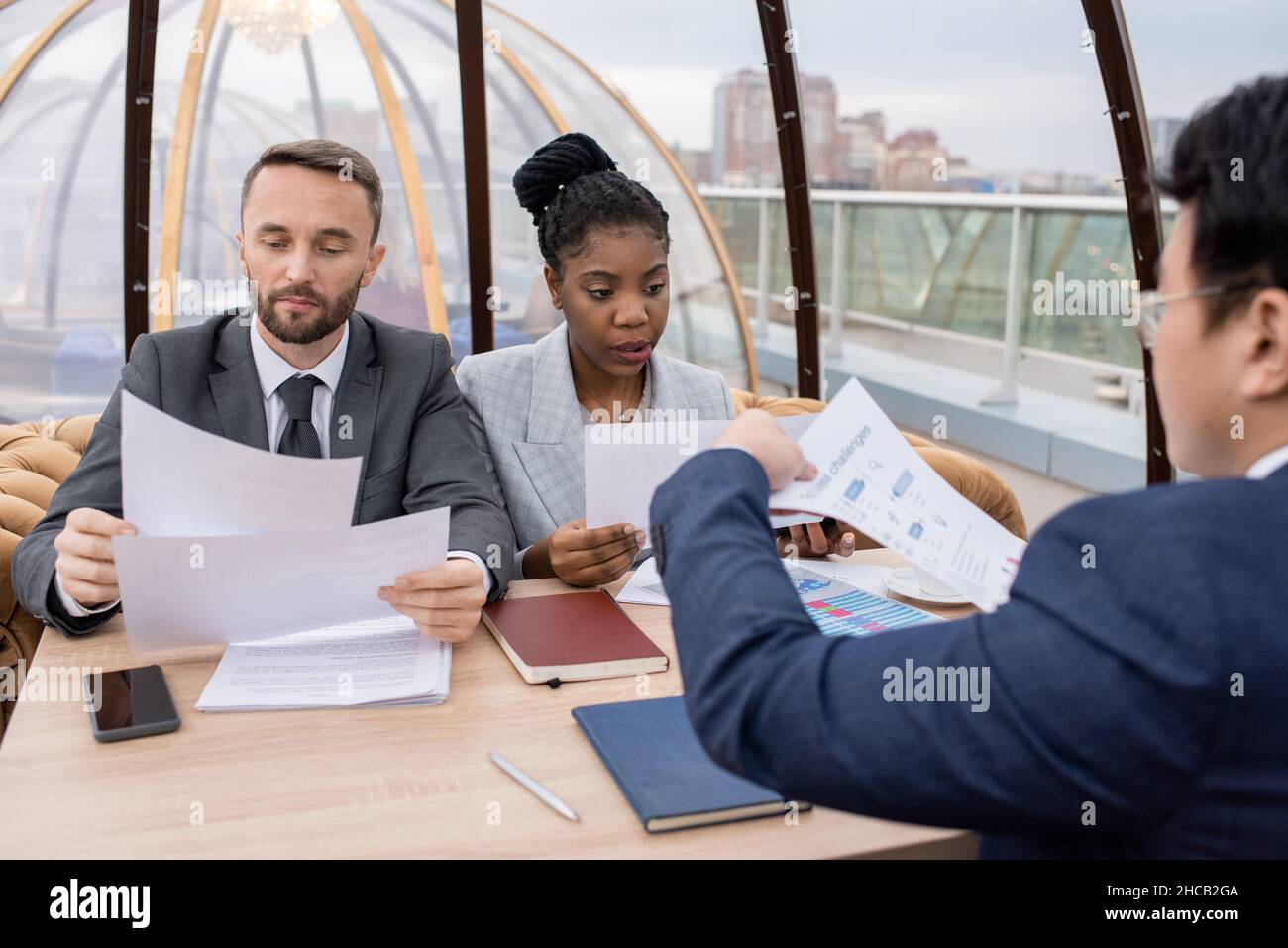 Two young serious colleagues looking through papers at working meeting ...