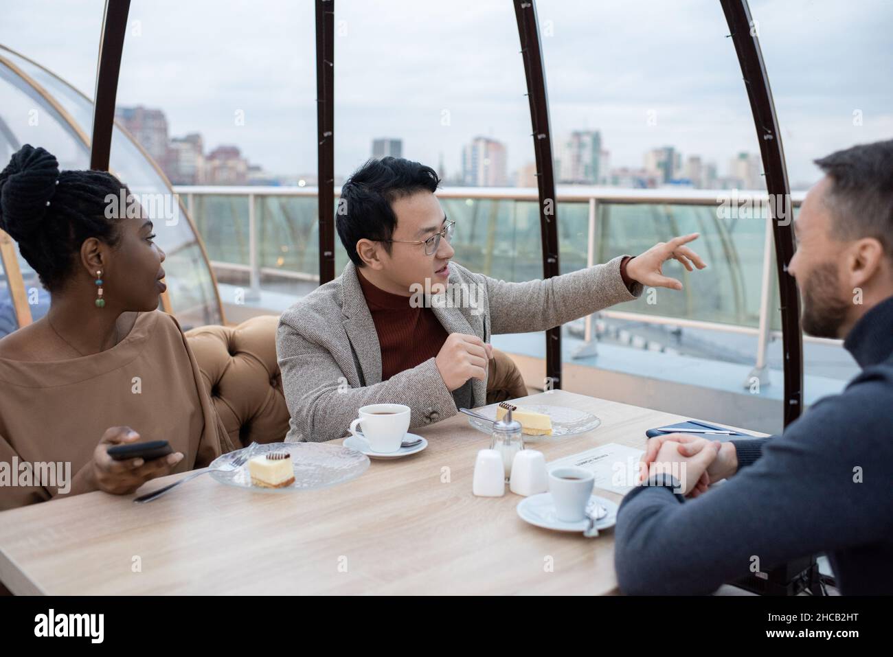 Contemporary young colleagues having discussion by dessert while one of ...