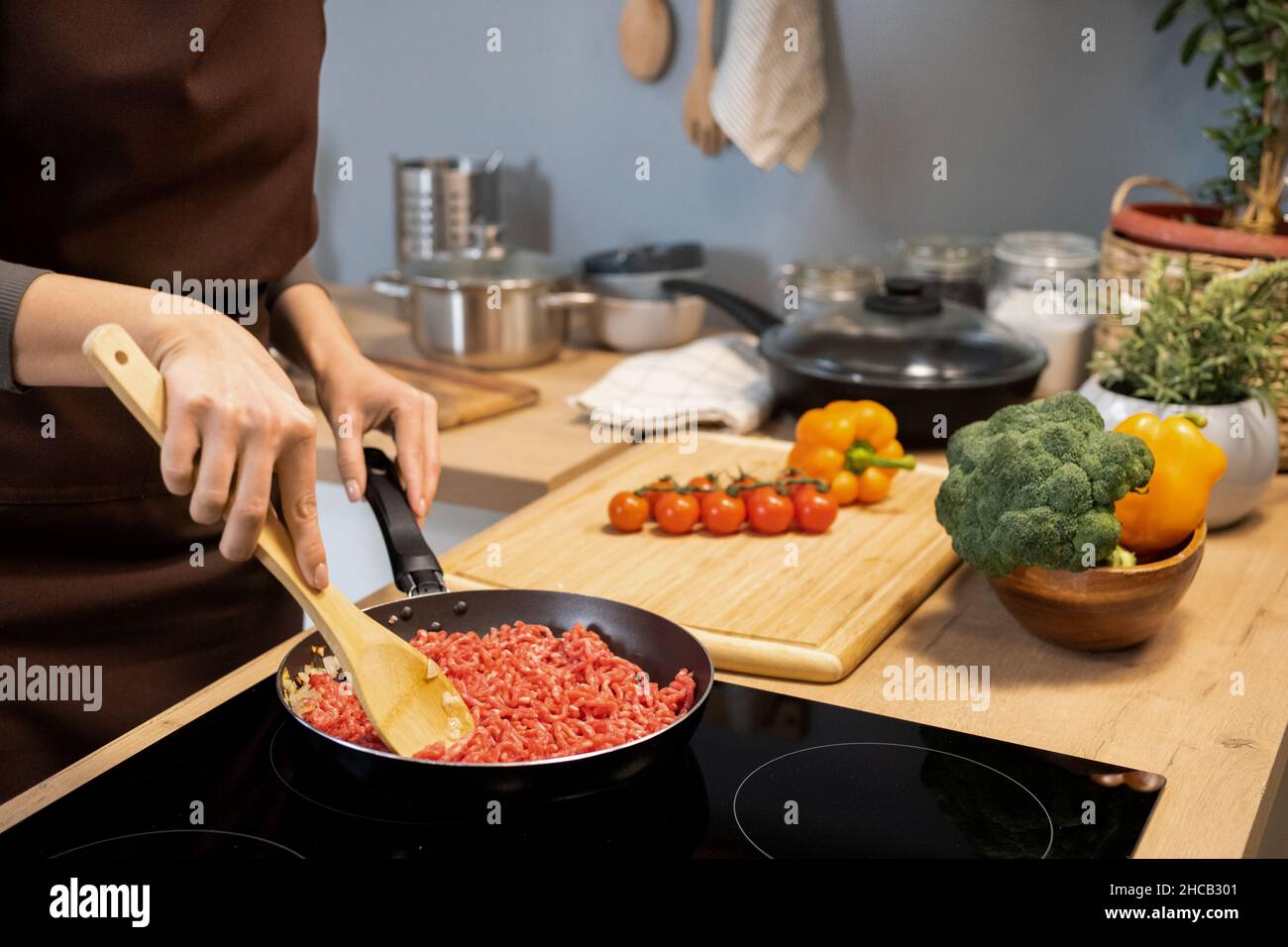 Young housewife mixing minced meat with wooden spoon in frying pan ...