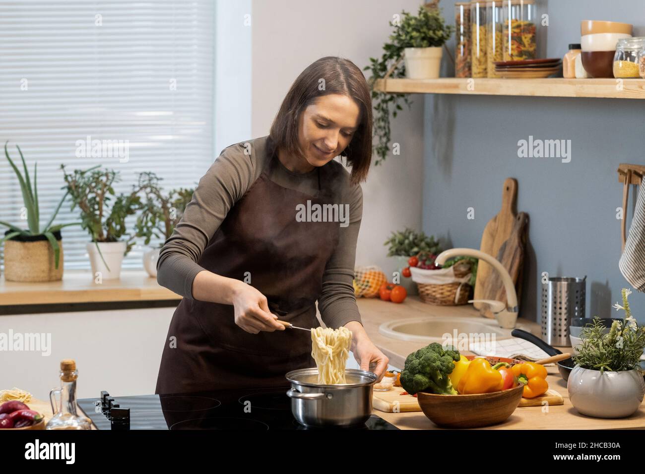 Happy young brunette female taking hot boiled spaghetti out of metallic ...