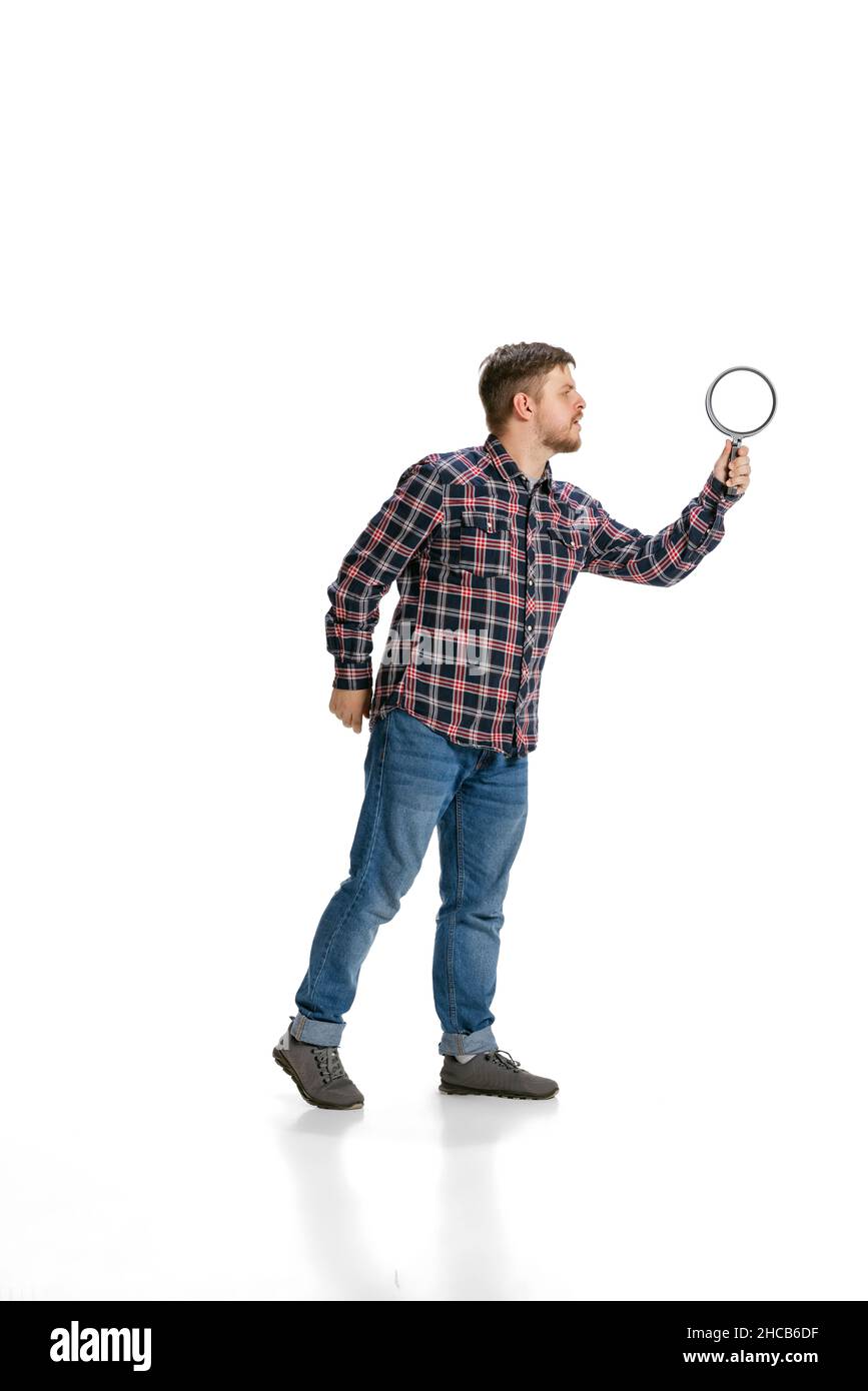 Full-length portrait of young man looking in magnifier isolated over ...