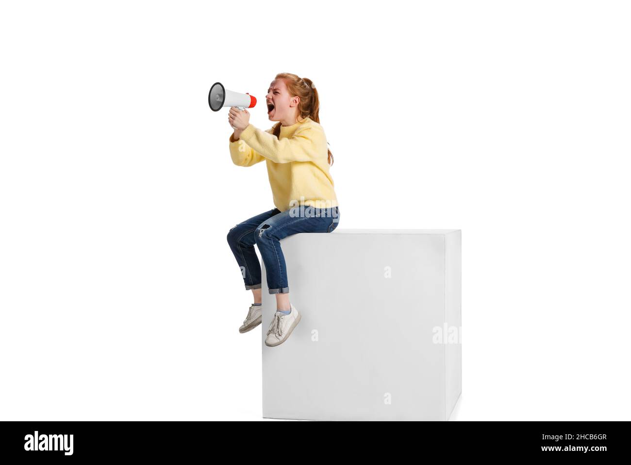 Full-length portrait of young girl shouting in megaphone with anger ...
