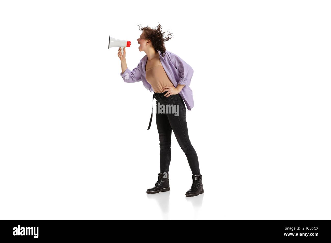 Full-length portrait of young angry girl shouting in megaphone isolated ...