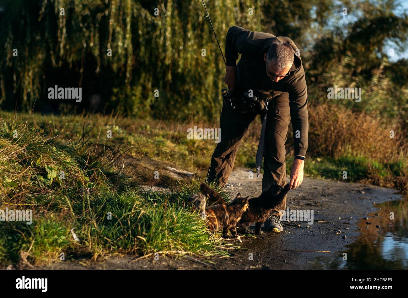 Fisherman with spinning rod gives the cat a fish perch on nature ...