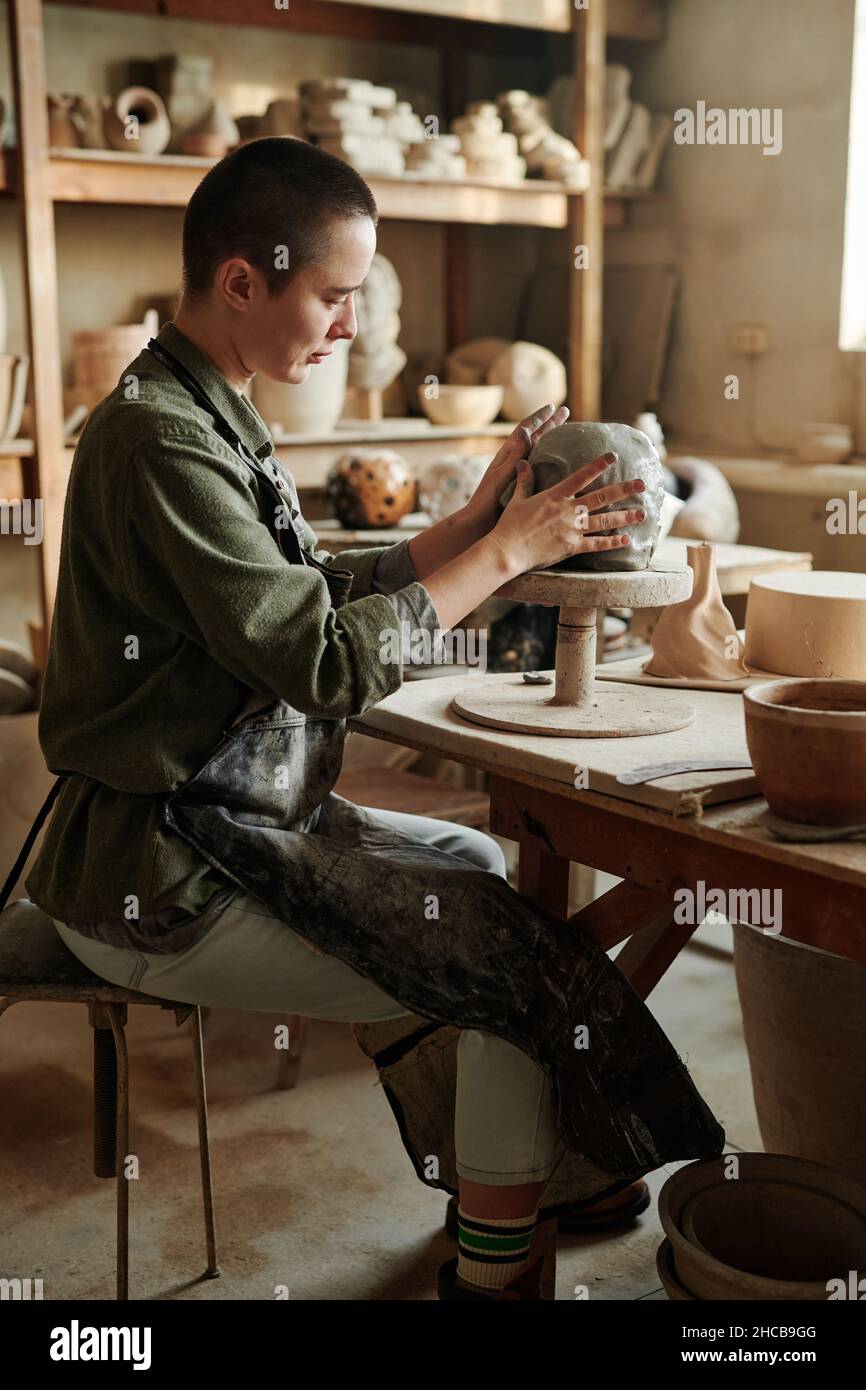 Sculptor sitting at the table using special equipment to make form of ...