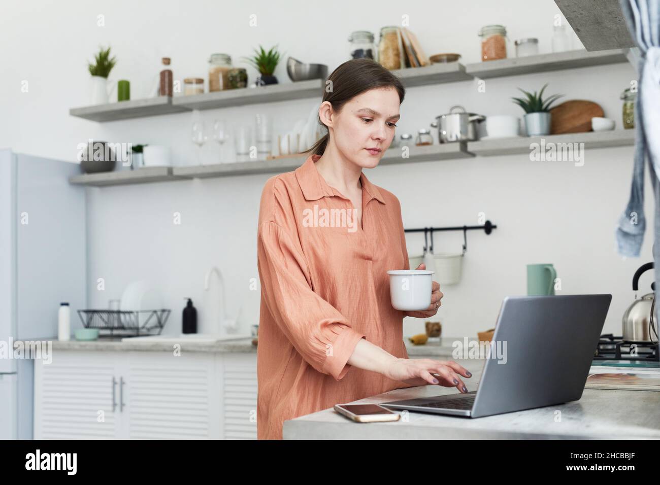 Young woman working online using her laptop while drinking coffee in ...