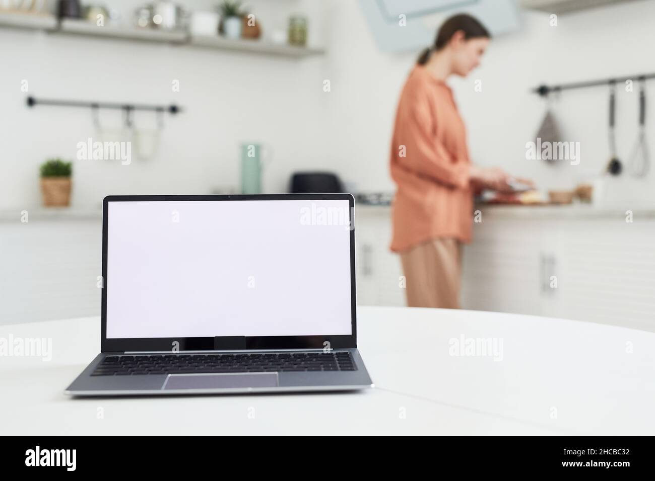 Close-up of laptop with empty screen on the kitchen table with woman ...