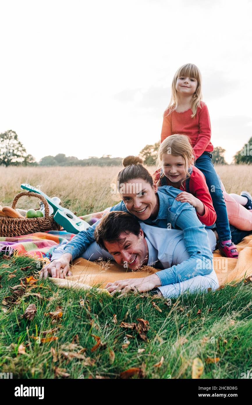 Playful parents with daughters lying down on blanket in park Stock ...
