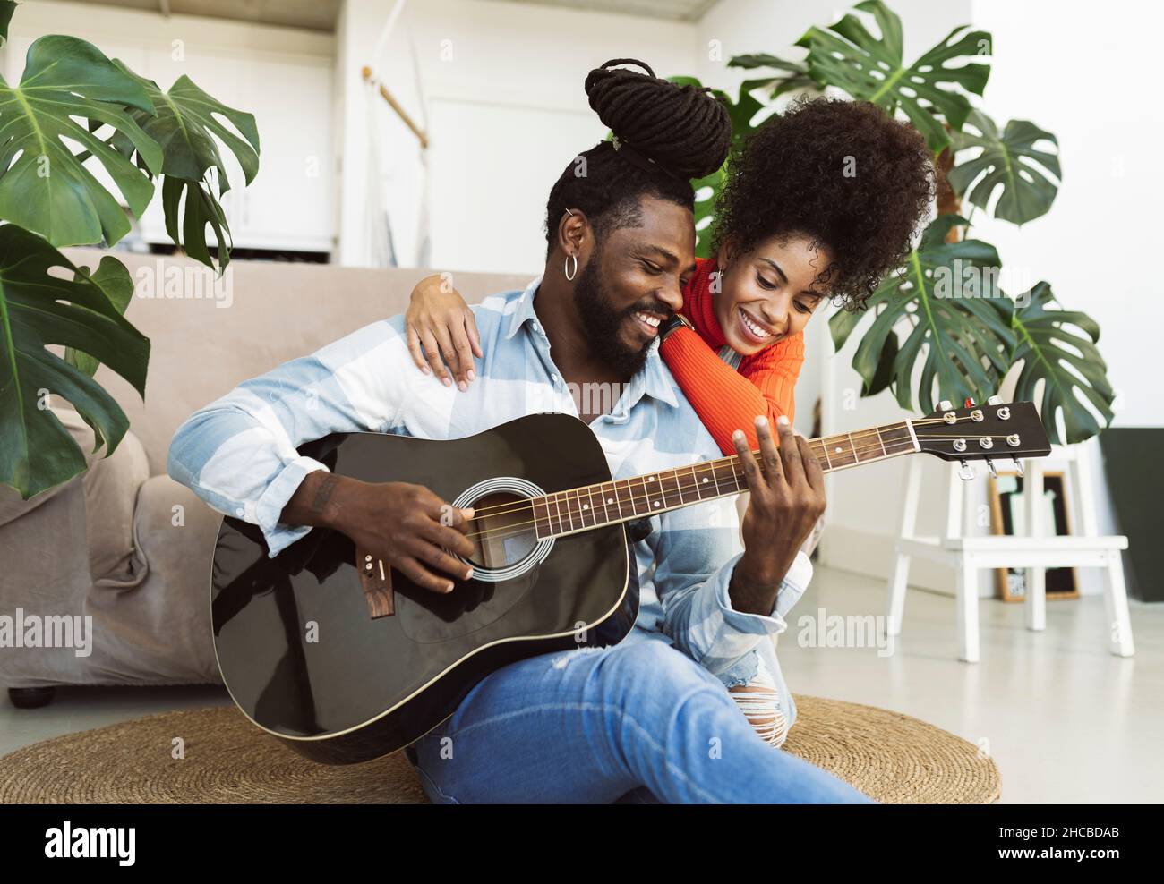 Young woman embracing boyfriend playing guitar in living room Stock ...