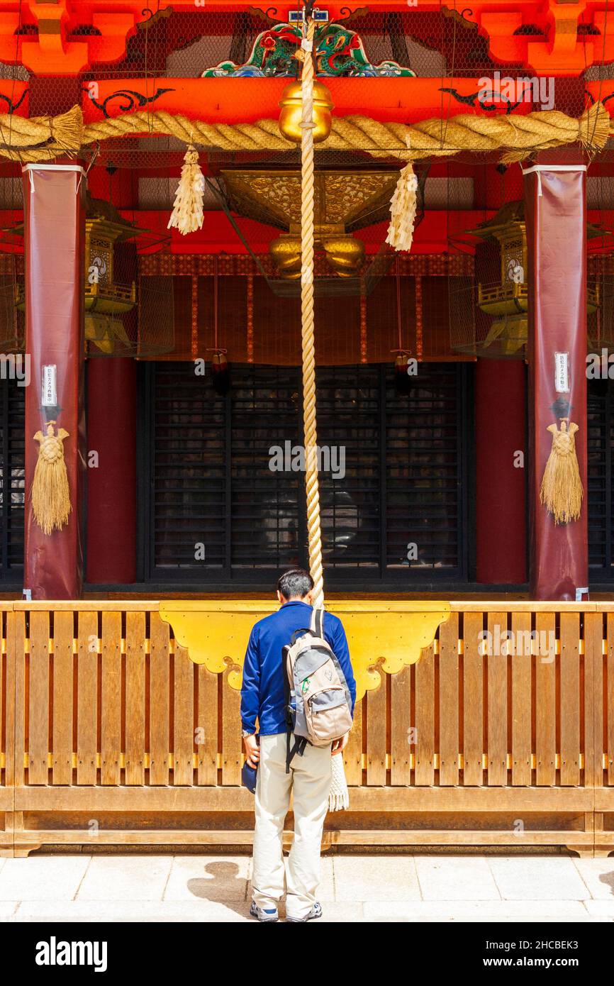 Man standing, bowing and praying in front of bell rope and large wooden ...