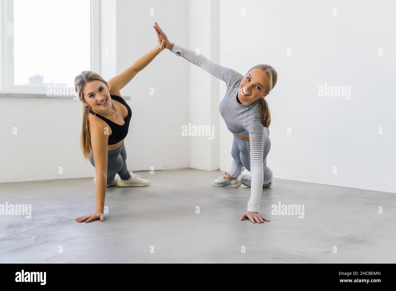 Young women practicing yoga together giving high five holding hands and ...