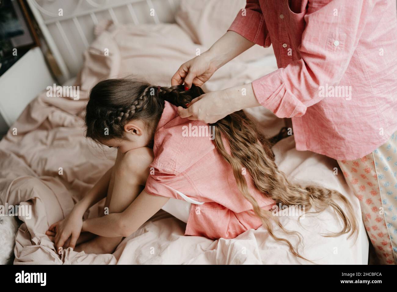 Mother braiding daughter's hair on bed at home Stock Photo - Alamy