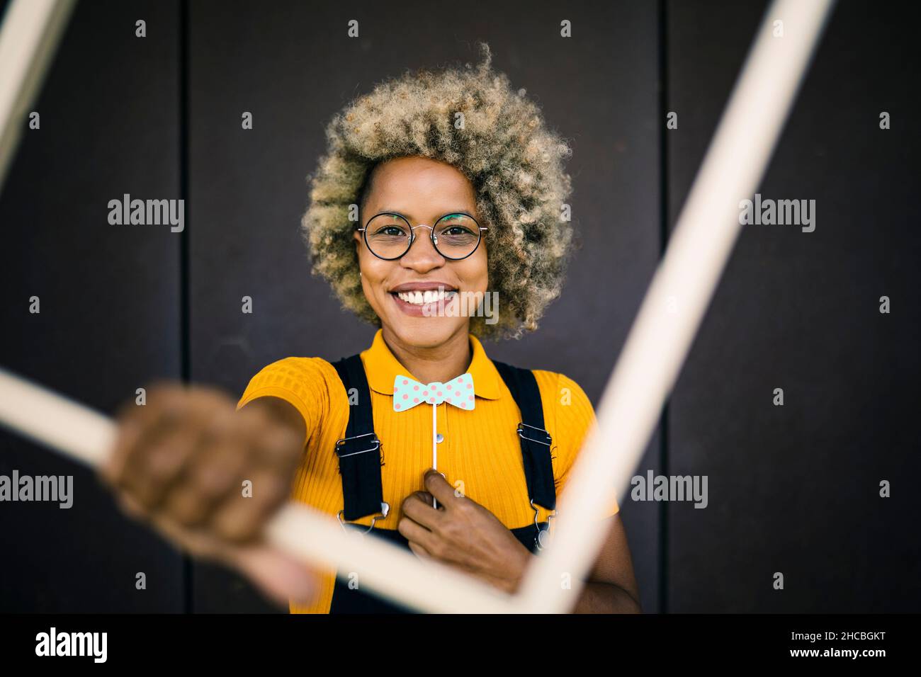 Smiling woman holding prop in front of black wall Stock Photo - Alamy