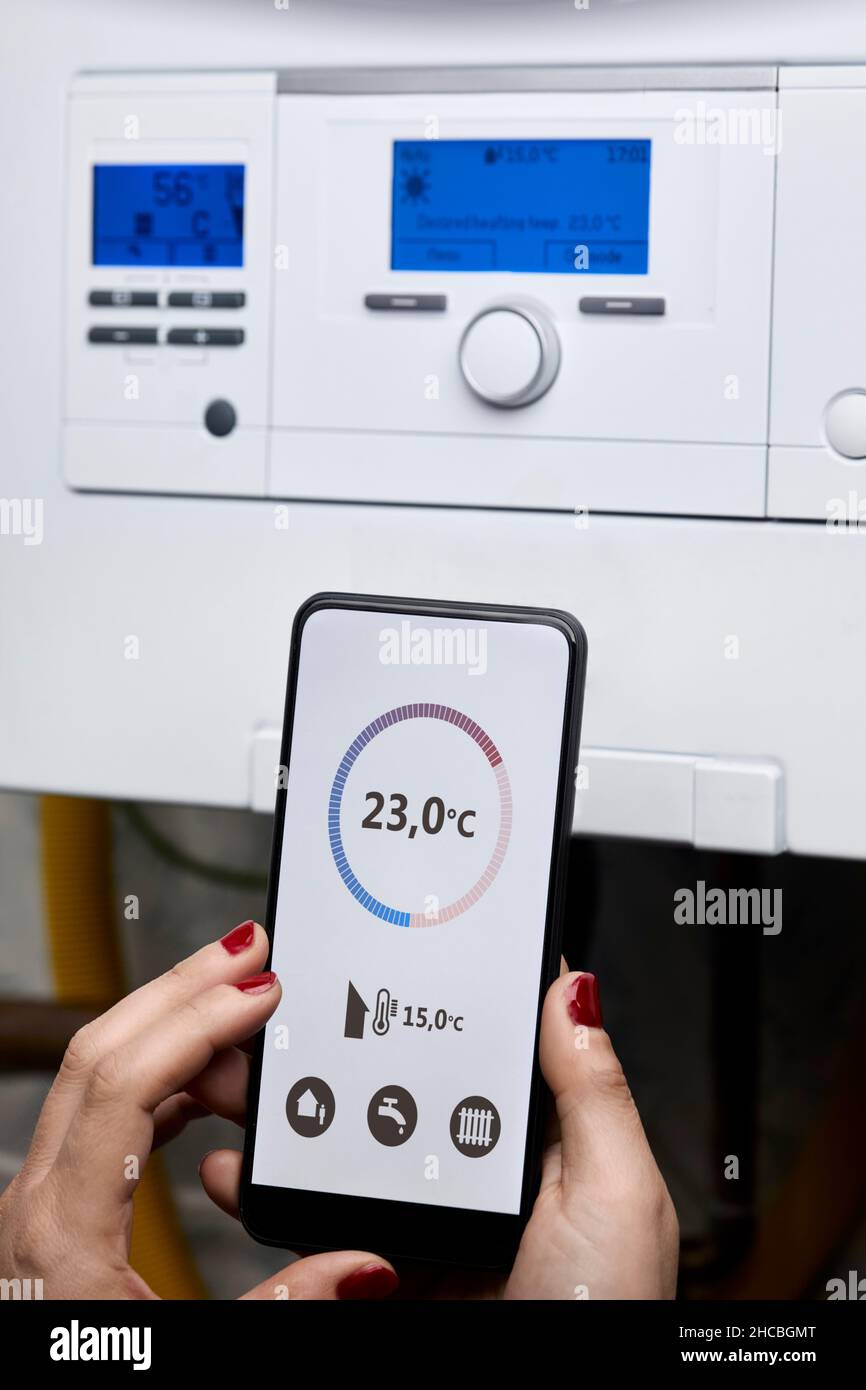 Woman adjusting temperature of heating boiler through mobile phone at ...
