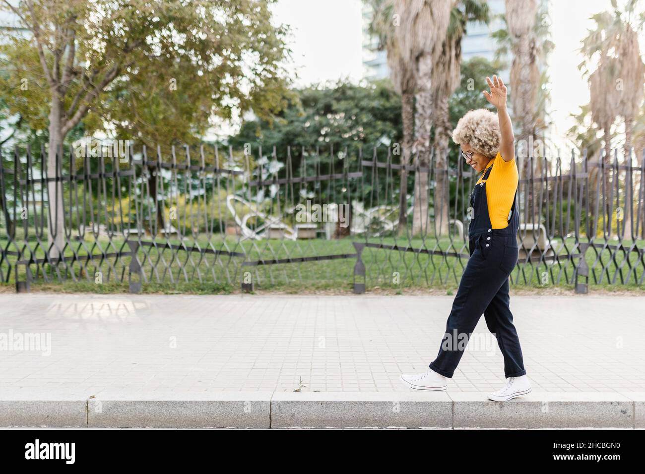 Carefree woman with arms outstretched walking at edge of sidewalk Stock ...