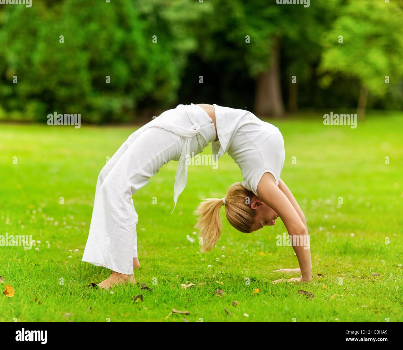Flexible blond woman performing wheel pose in park Stock Photo - Alamy