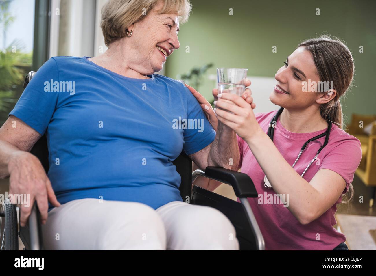 Nurse giving drinking water to woman in wheelchair at home Stock Photo ...