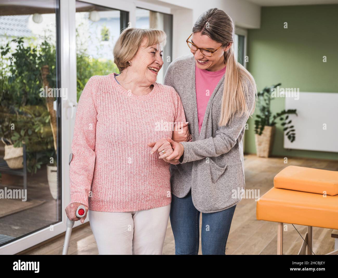 Smiling caregiver helping disabled woman to walk at home Stock Photo ...