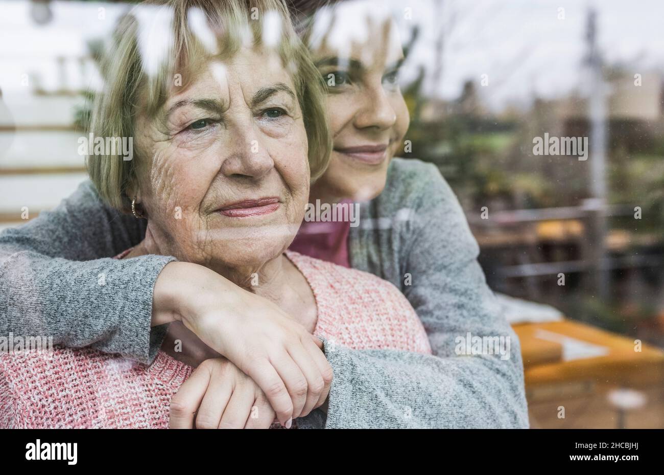 Caregiver hugging senior woman at window Stock Photo - Alamy