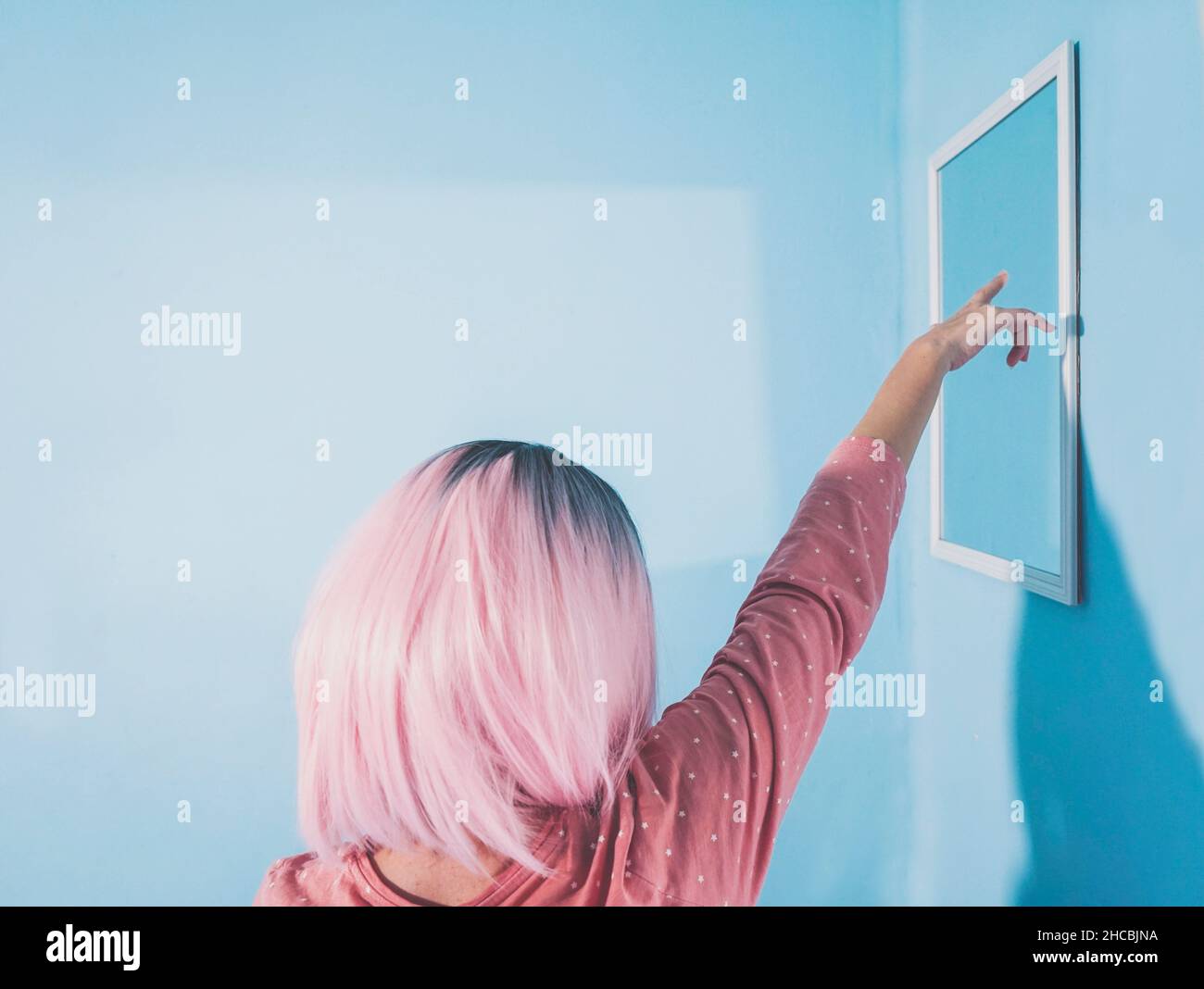 Woman with pink hair pointing at mirror on blue wall Stock Photo - Alamy