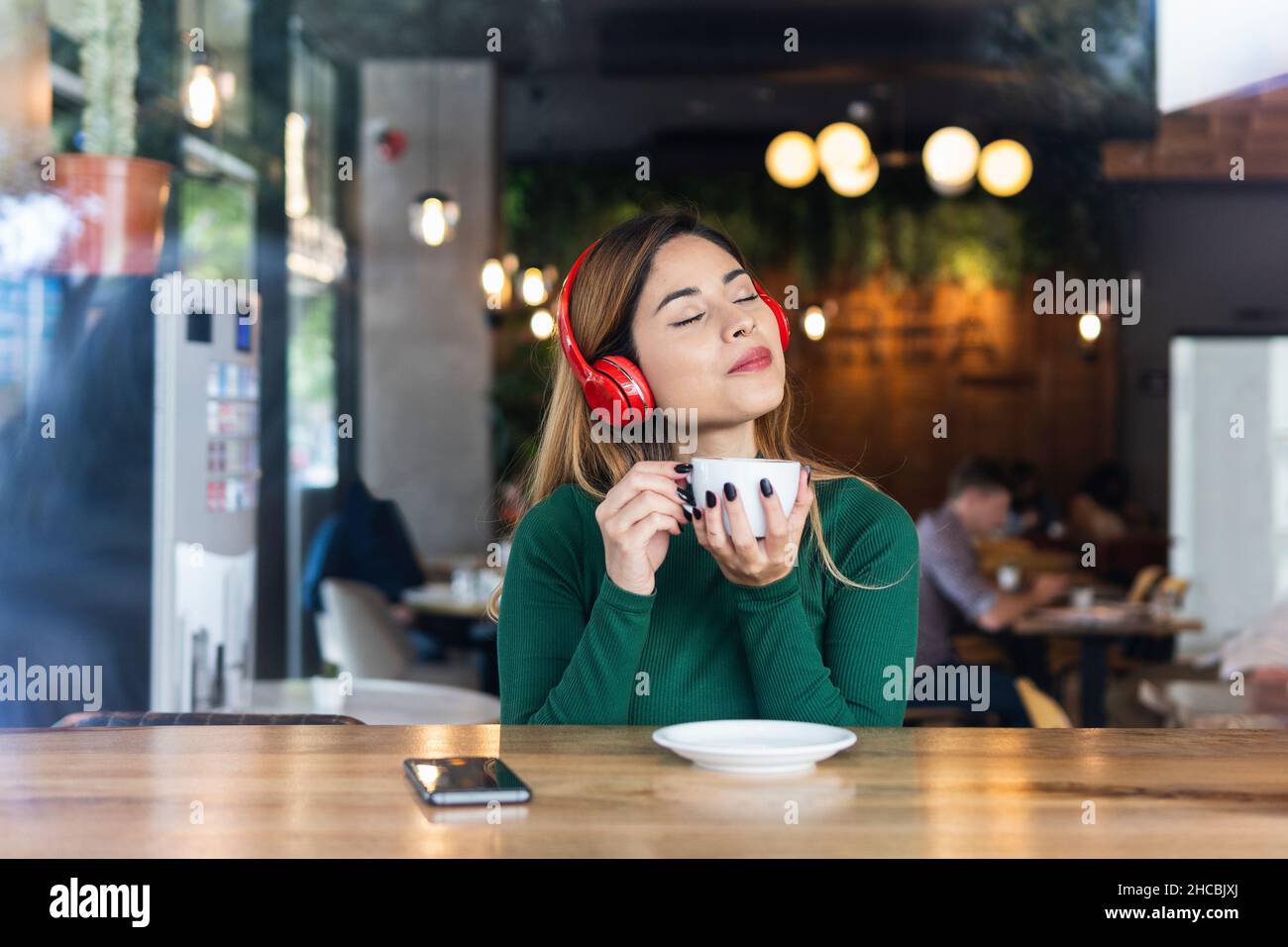 Woman with coffee cup listening music through headphones in cafe Stock ...