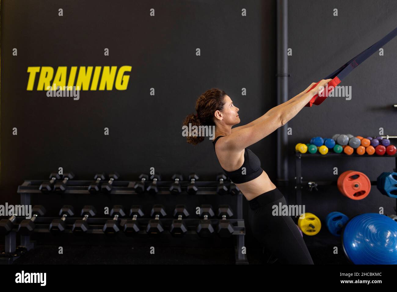 Sportswoman leaning backwards pulling straps in gym Stock Photo - Alamy