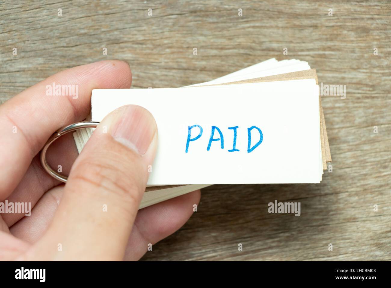 Man hold the flash card with handwriting word paid on wood background ...
