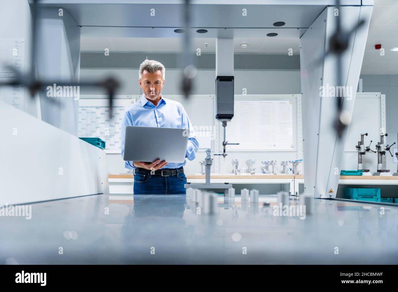 Engineer with laptop at automated manufacturing machinery in industry ...