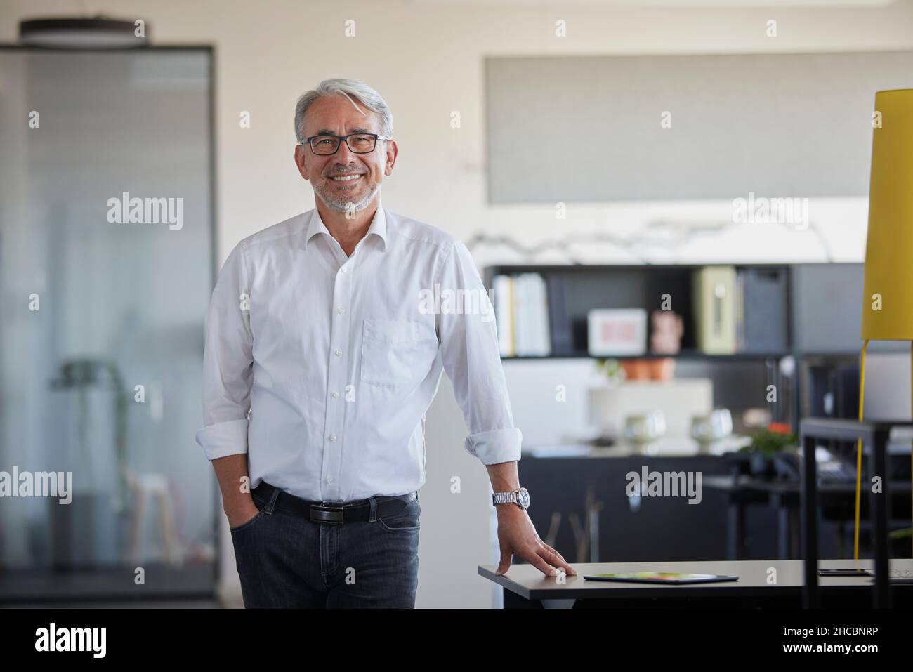 Happy mature businessman standing with hand in pocket at workplace ...