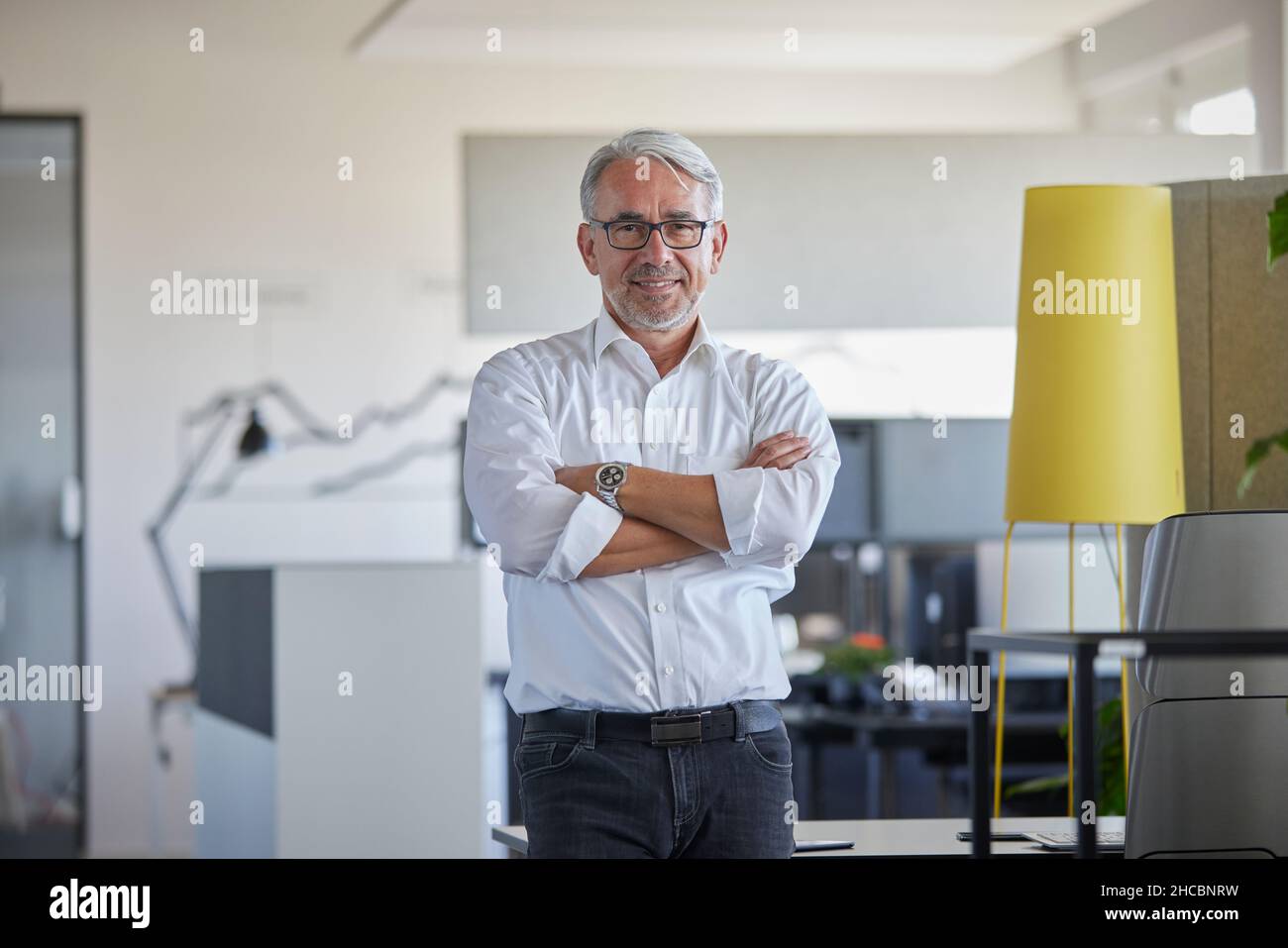 Smiling businessman standing with arms crossed at workplace Stock Photo ...