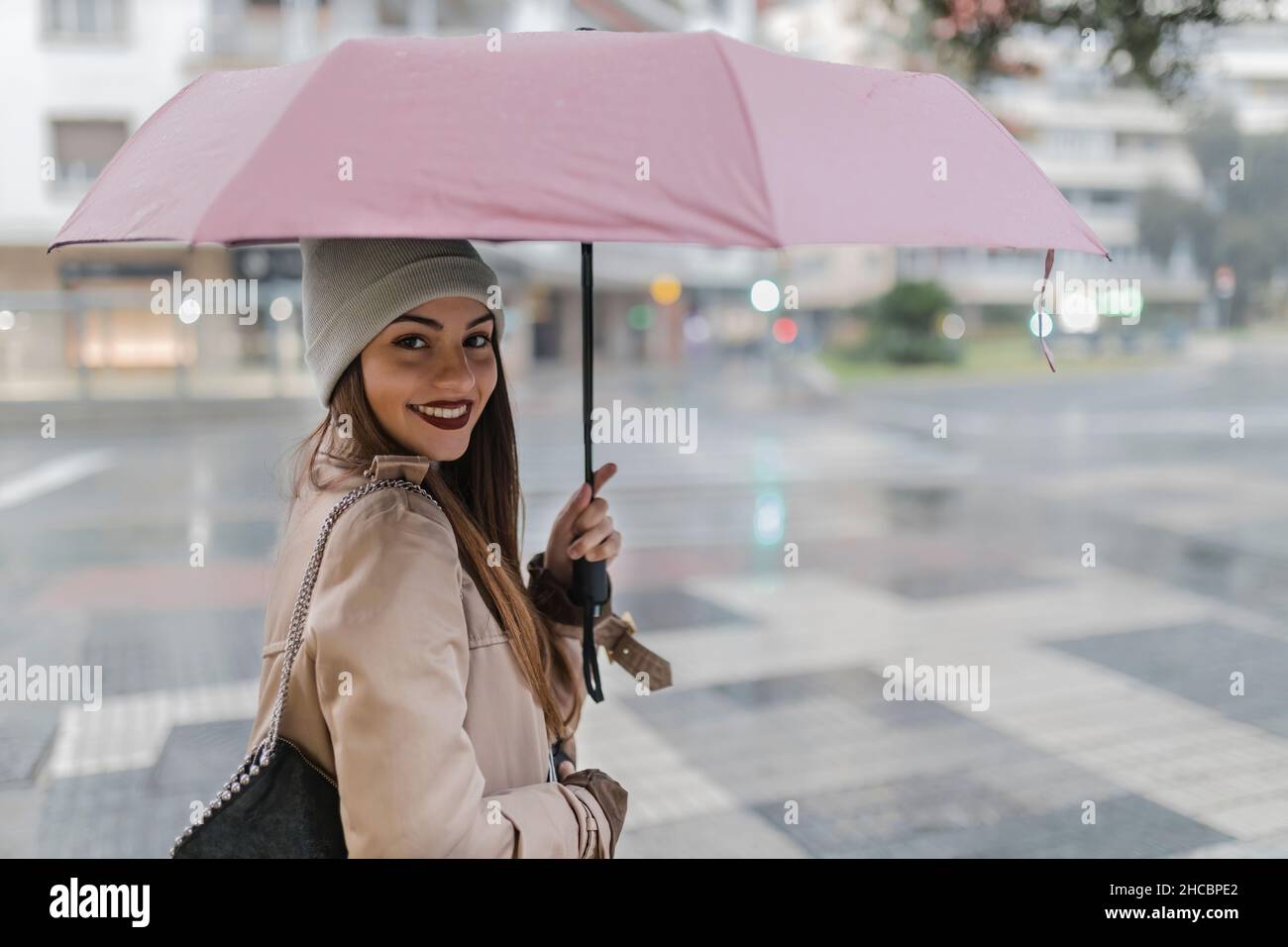 Woman looking over shoulder holding umbrella at city street Stock Photo ...